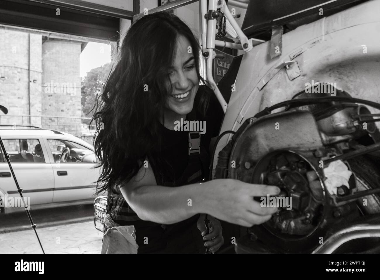 A cheerful female mechanic works on a moped italian vintage scooter ...