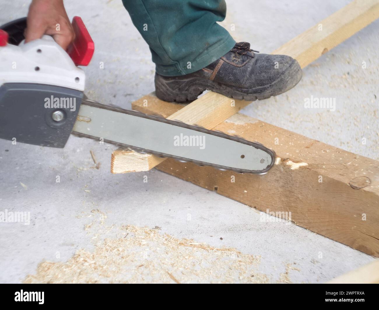 Worker sawing a wooden plank with a chainsaw on a construction site ...