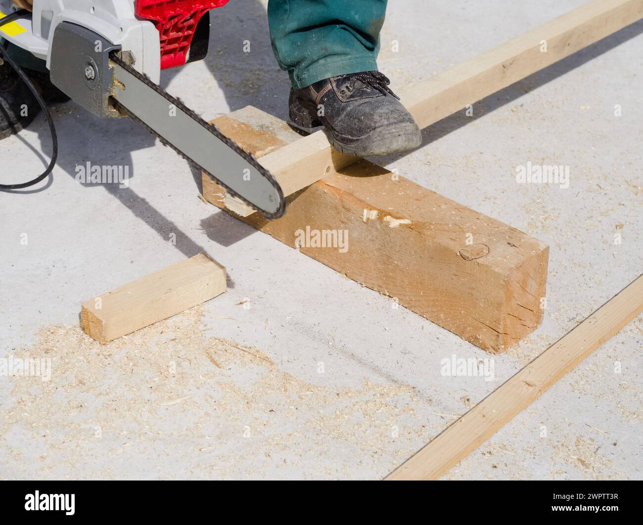 Worker sawing a wooden plank with a chainsaw on a construction site ...