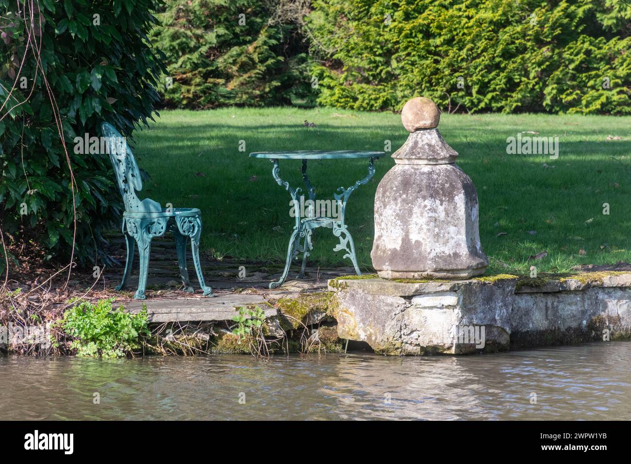 Riverside garden with garden chair and table on lawn beside the water ...