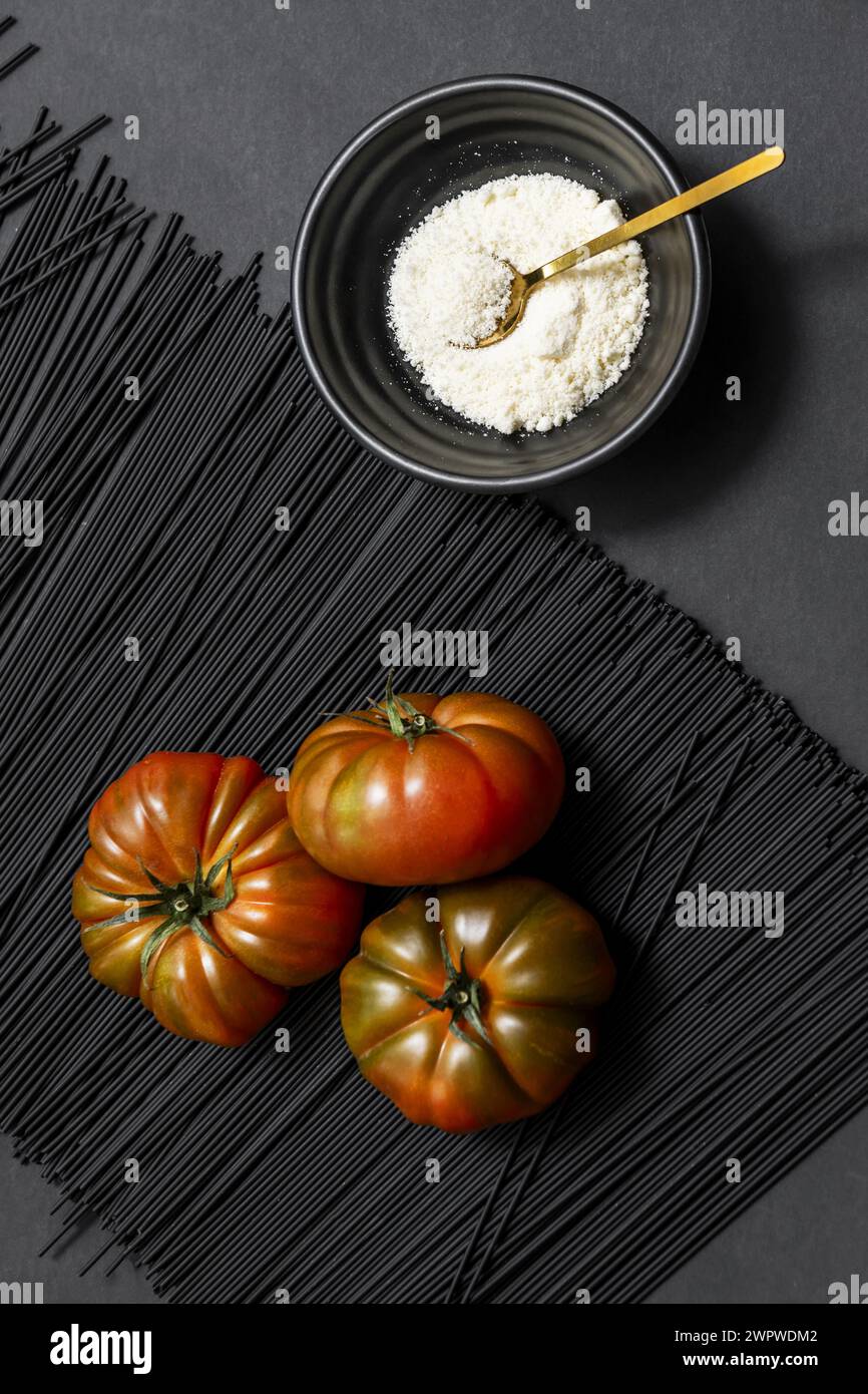 A trio of succulent ripe Raf tomatoes on a mound of black pasta next to ...