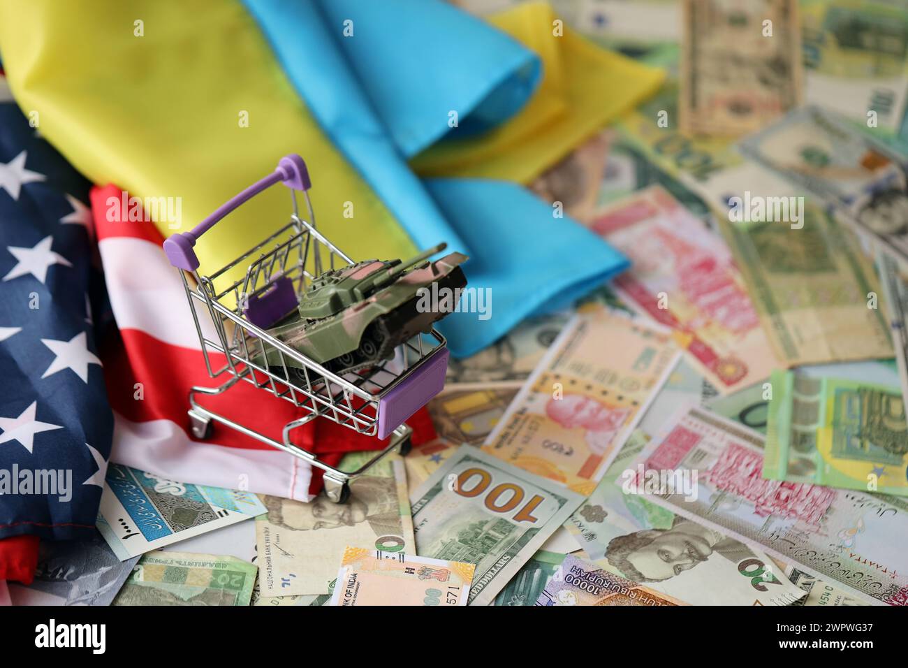 Toy tank on US flag and ukrainian flag on many banknotes of different ...