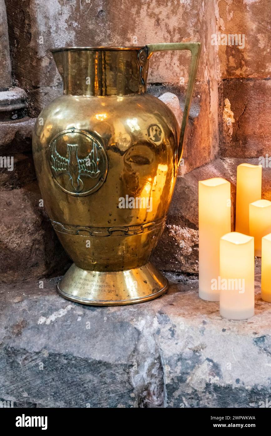 Still life with antique brass jug, lit candles set against ancient ...