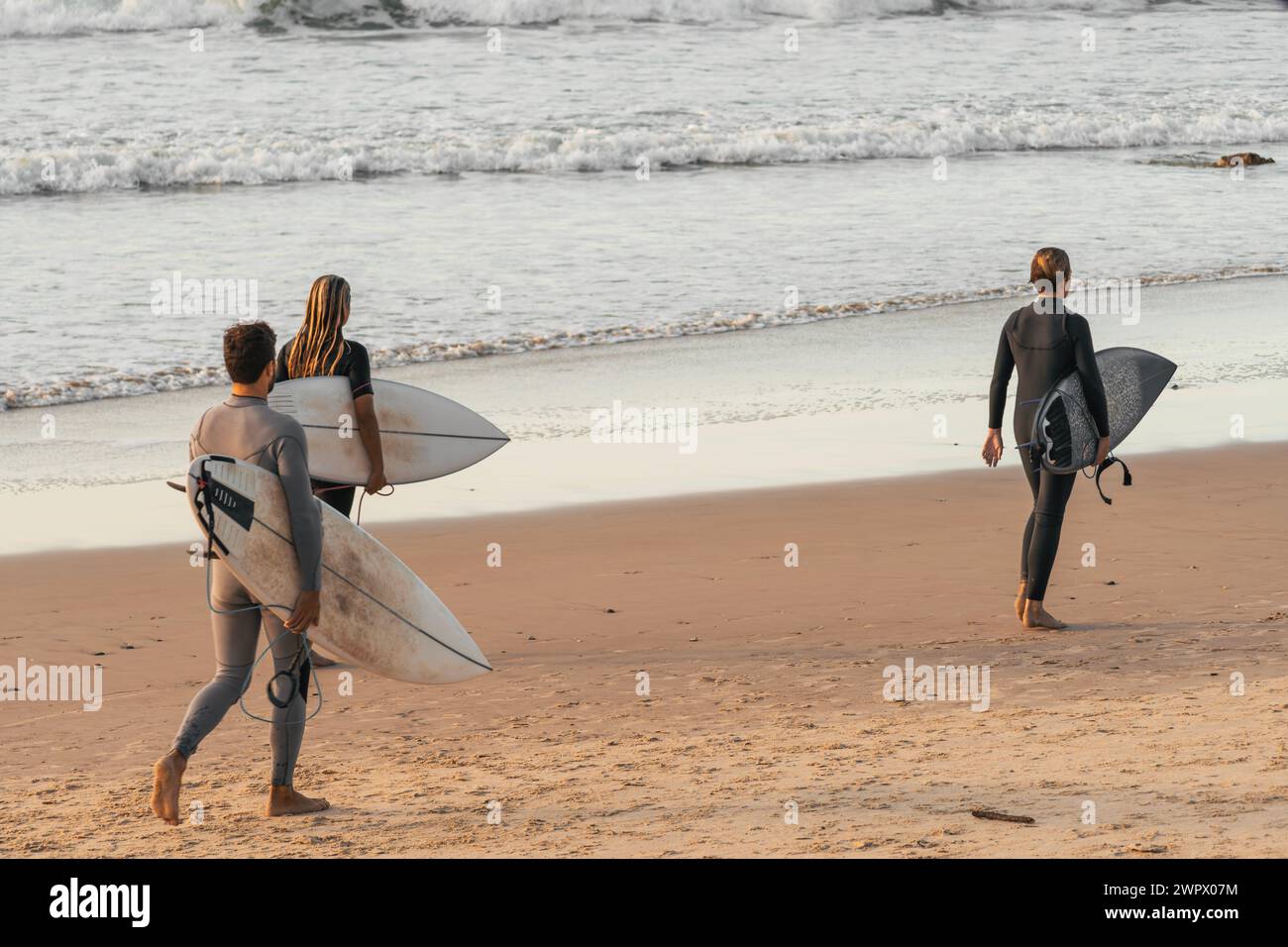Three surfers walking along the beach with their surfboards dressed in ...