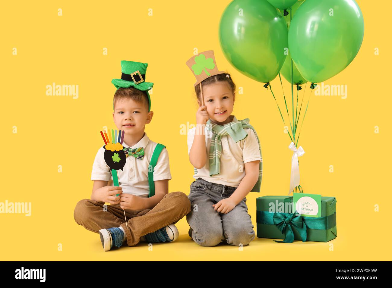Cute kids with festive green outfits and balloons on yellow background ...