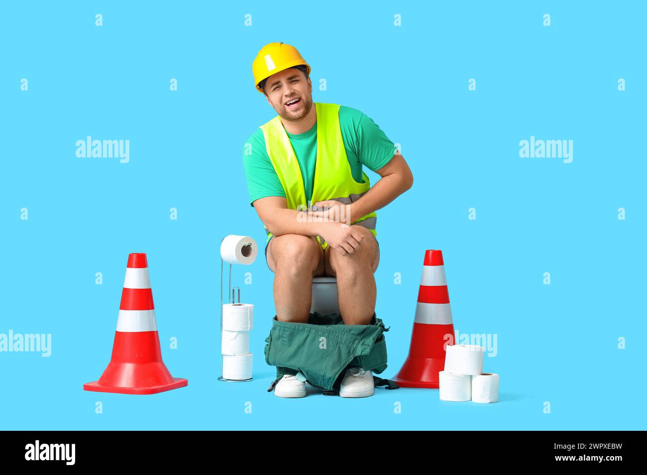Male worker sitting on toilet bowl with traffic cones against blue ...
