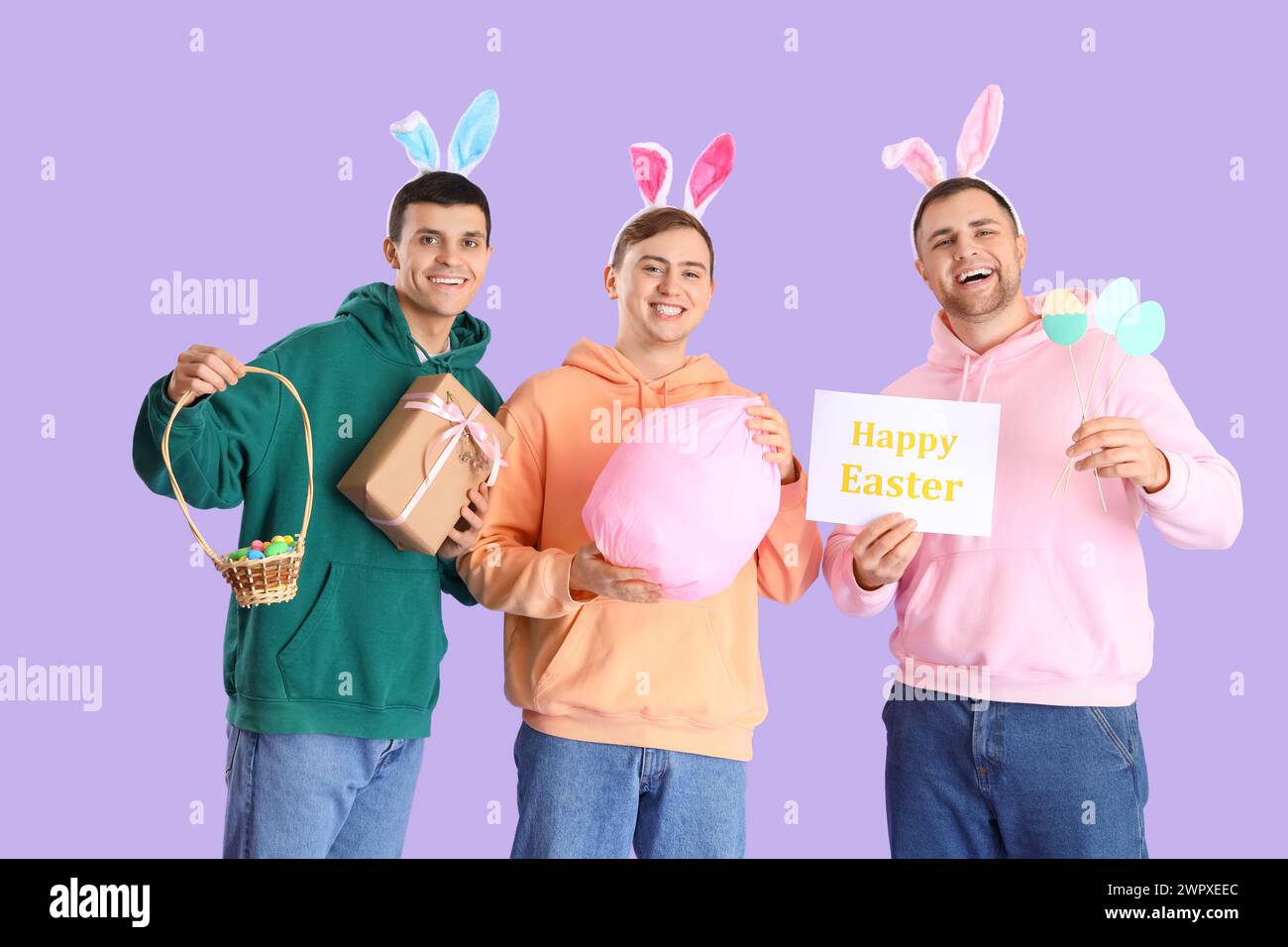 Happy young men in bunny ears celebrating Easter on purple background ...