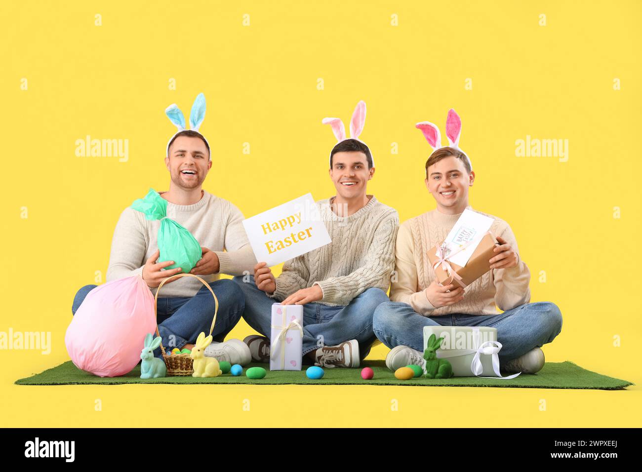Happy young men in bunny ears celebrating Easter on yellow background ...