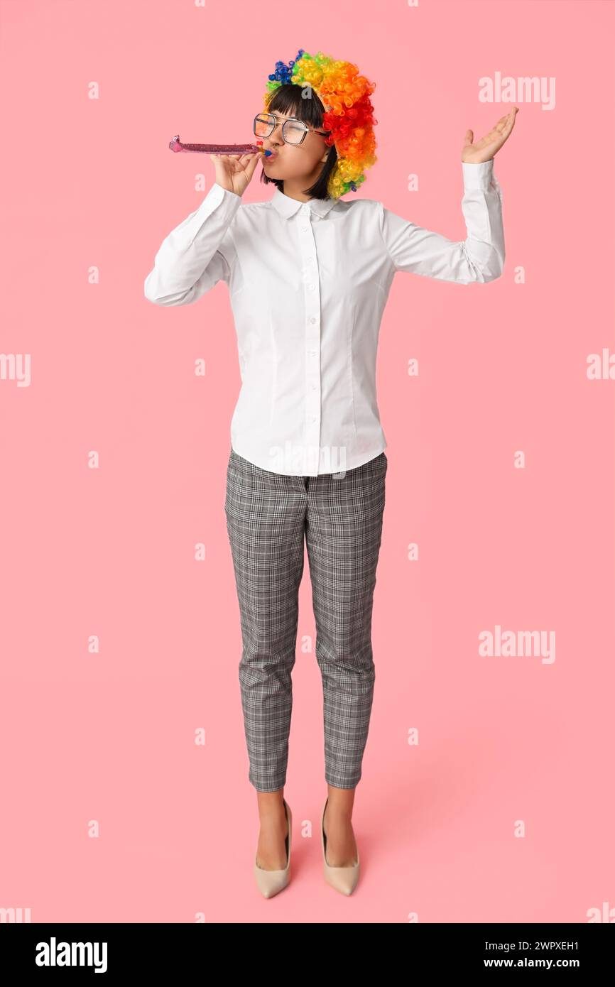 Funny young businesswoman with party blower on pink background. Fool's ...