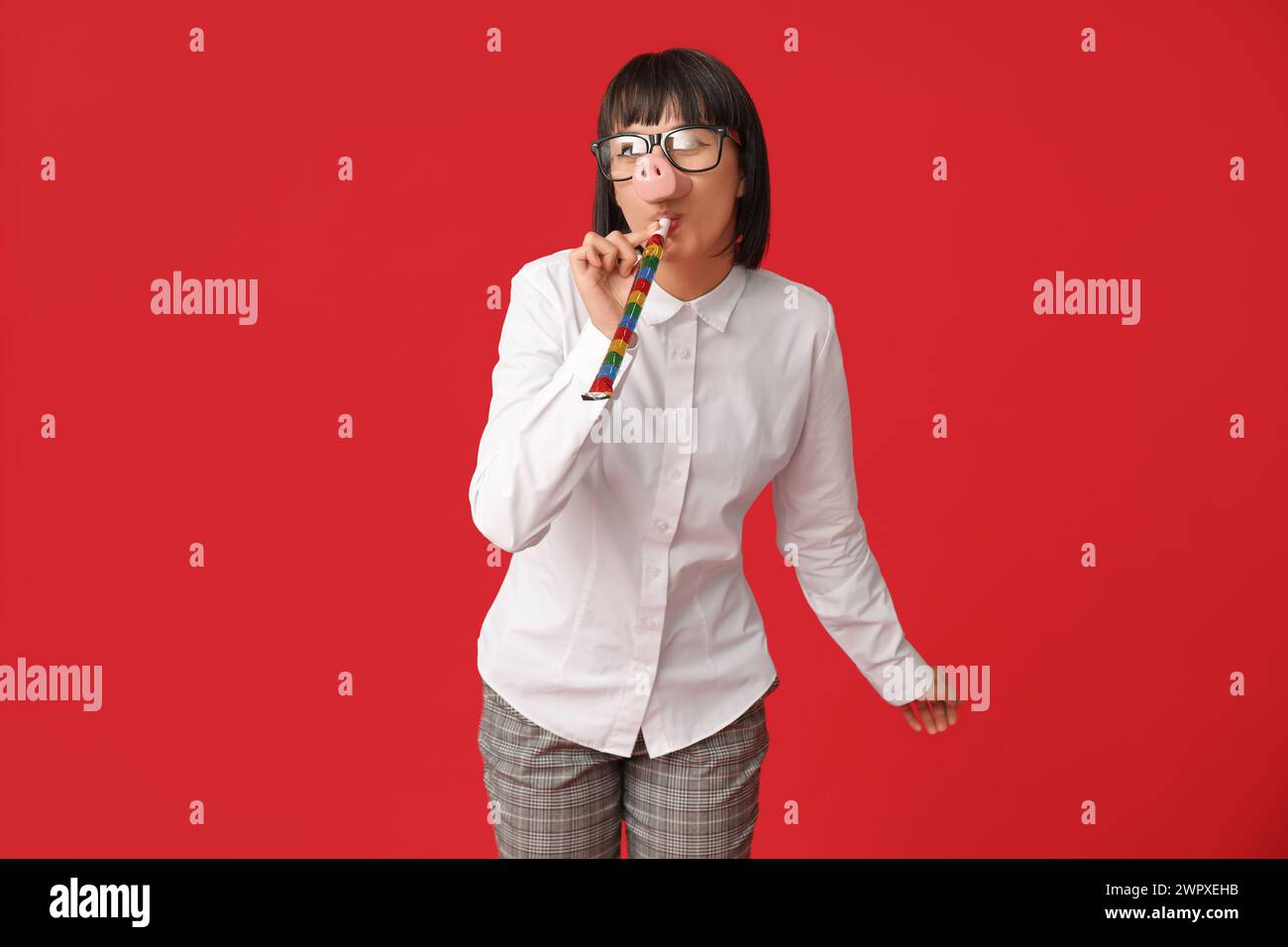 Funny young businesswoman with party blower on red background. Fool's ...