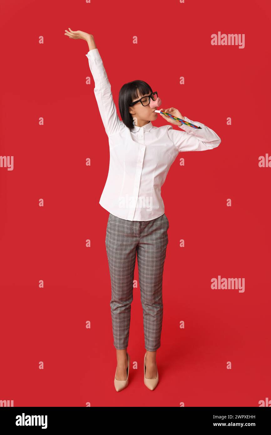 Funny young businesswoman with party blower on red background. Fool's ...