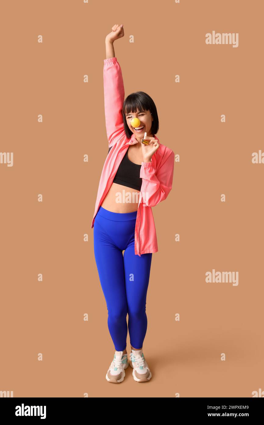 Funny young female fitness trainer with party blower on beige ...