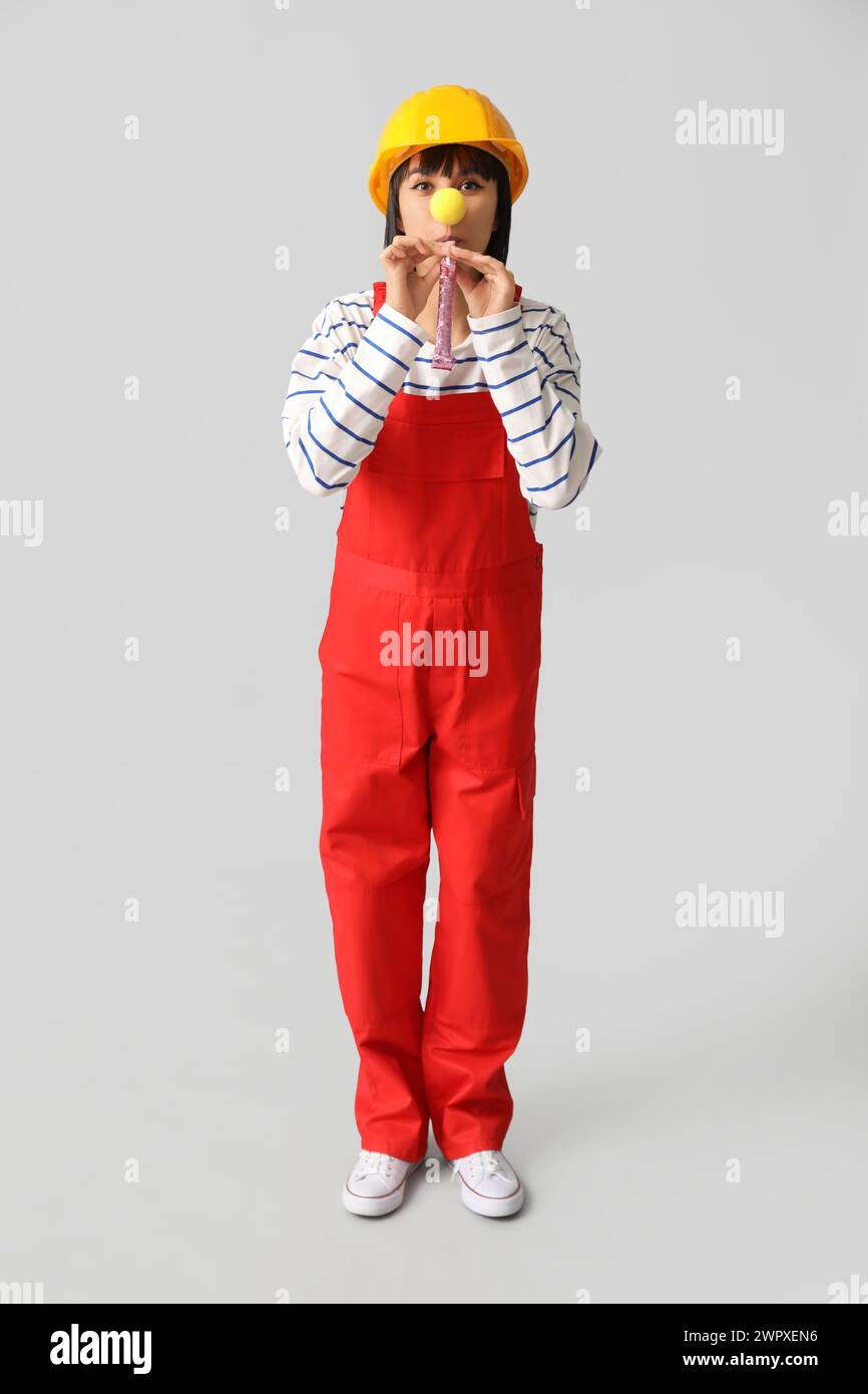 Funny young female builder with hardhat and party blower on white ...