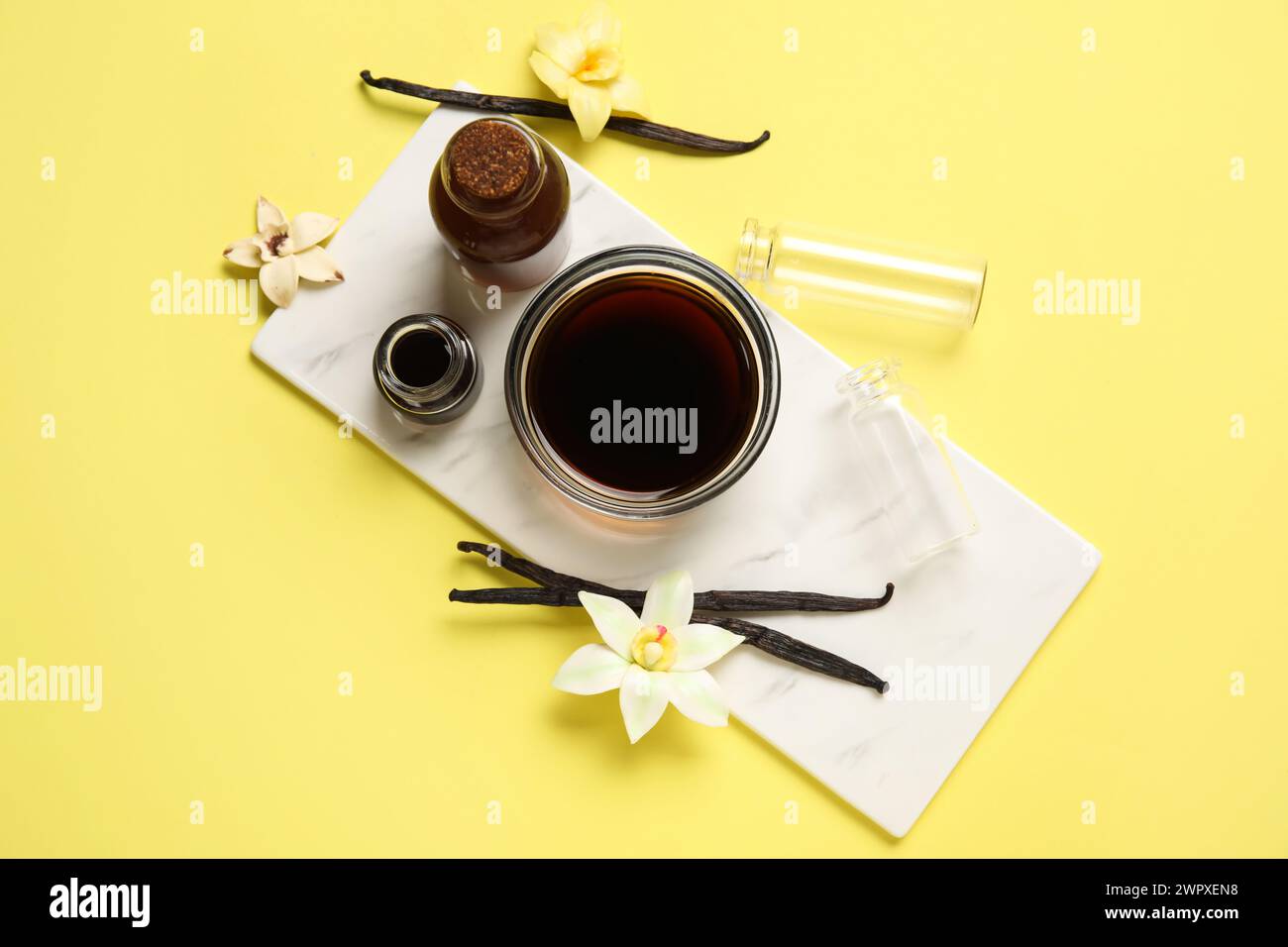 Vanilla extract in bottles, vanilla pods and flowers on yellow ...