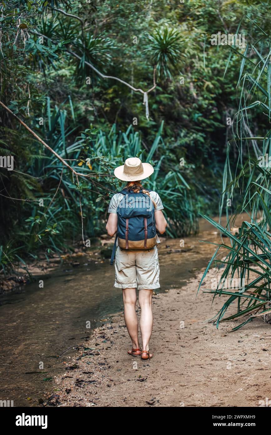 Young woman in beige shirt, shorts and straw haw, backpack on shoulders ...
