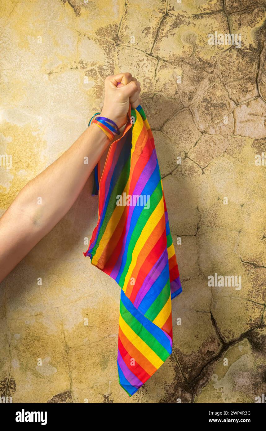 Feminine hand with rainbow bracelet tightly gripping a lgbt flag ...