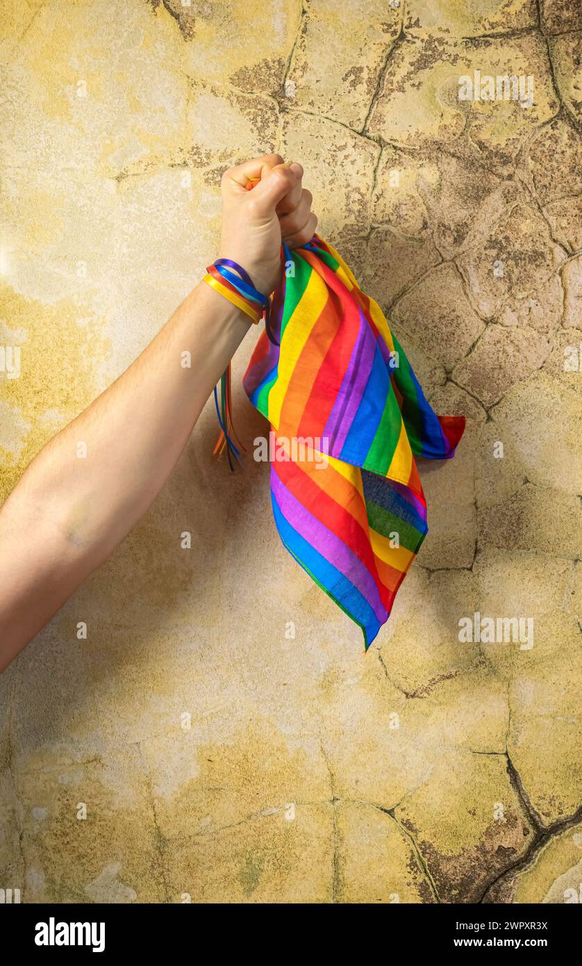 Feminine hand with rainbow bracelet tightly gripping a lgbt flag ...