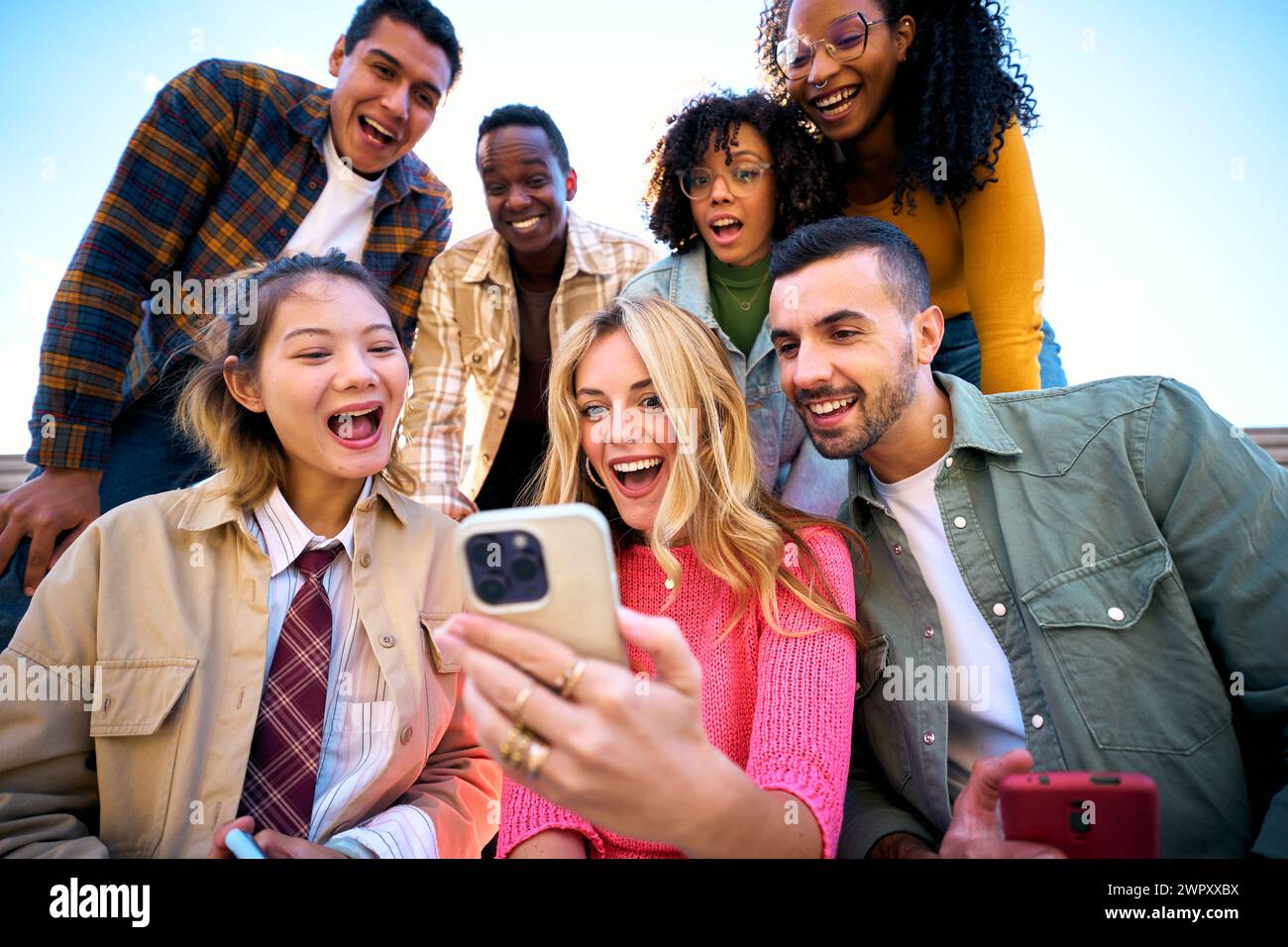 A group of happy amazed humans friends in outerwear using mobile ...