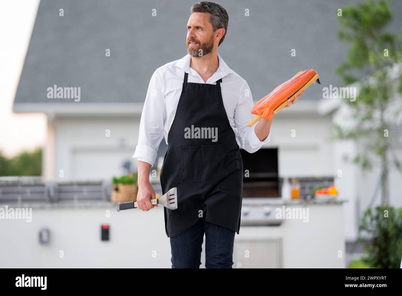 Hispanic man in cook apron cooking salmon fish on barbecue in the ...