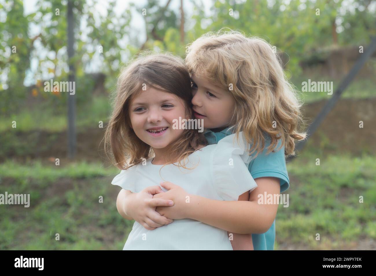 Two little children hug and kiss each other in summer garden. Kids ...