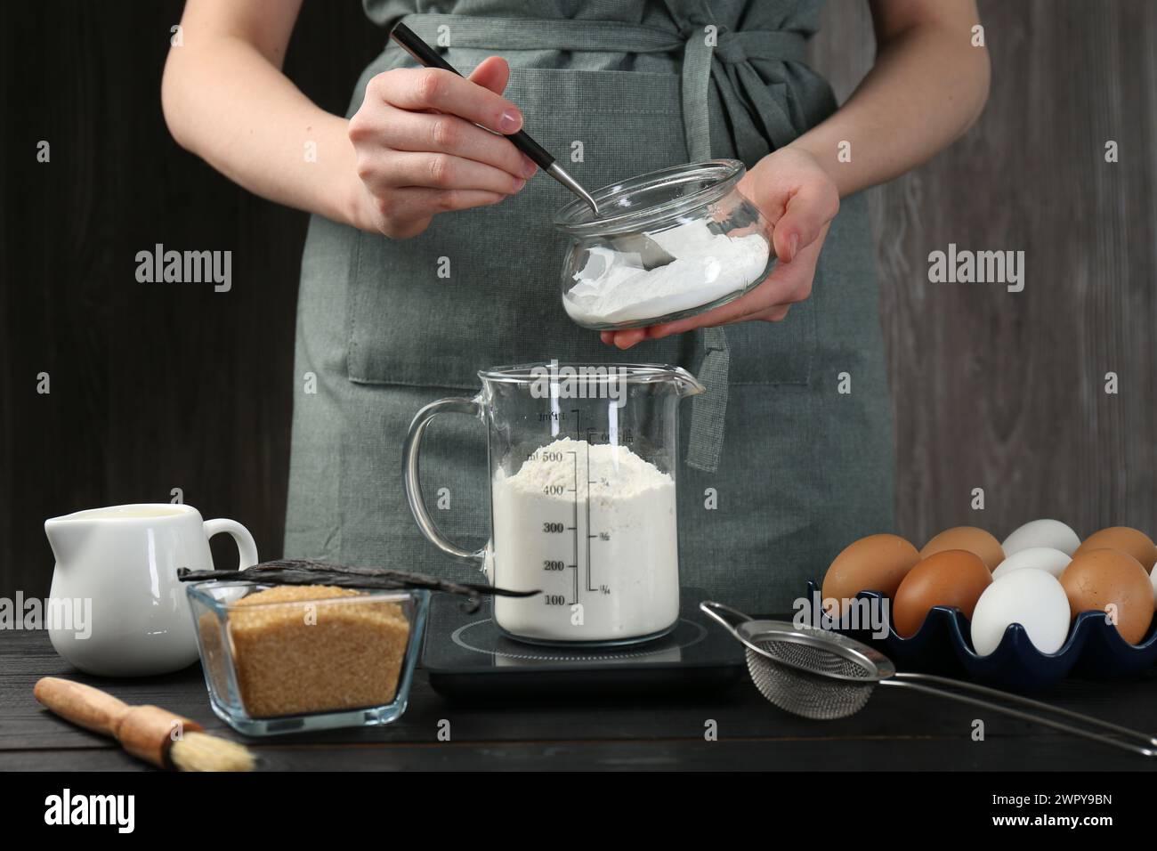 Woman adding baking powder into measuring cup at black wooden table ...