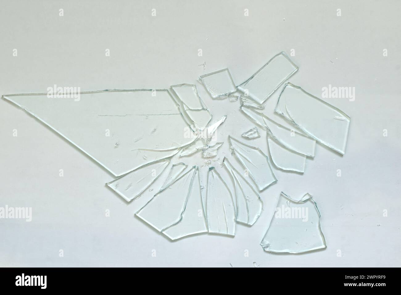 Sharp glass fragments of different sizes lie chaotically on a white ...