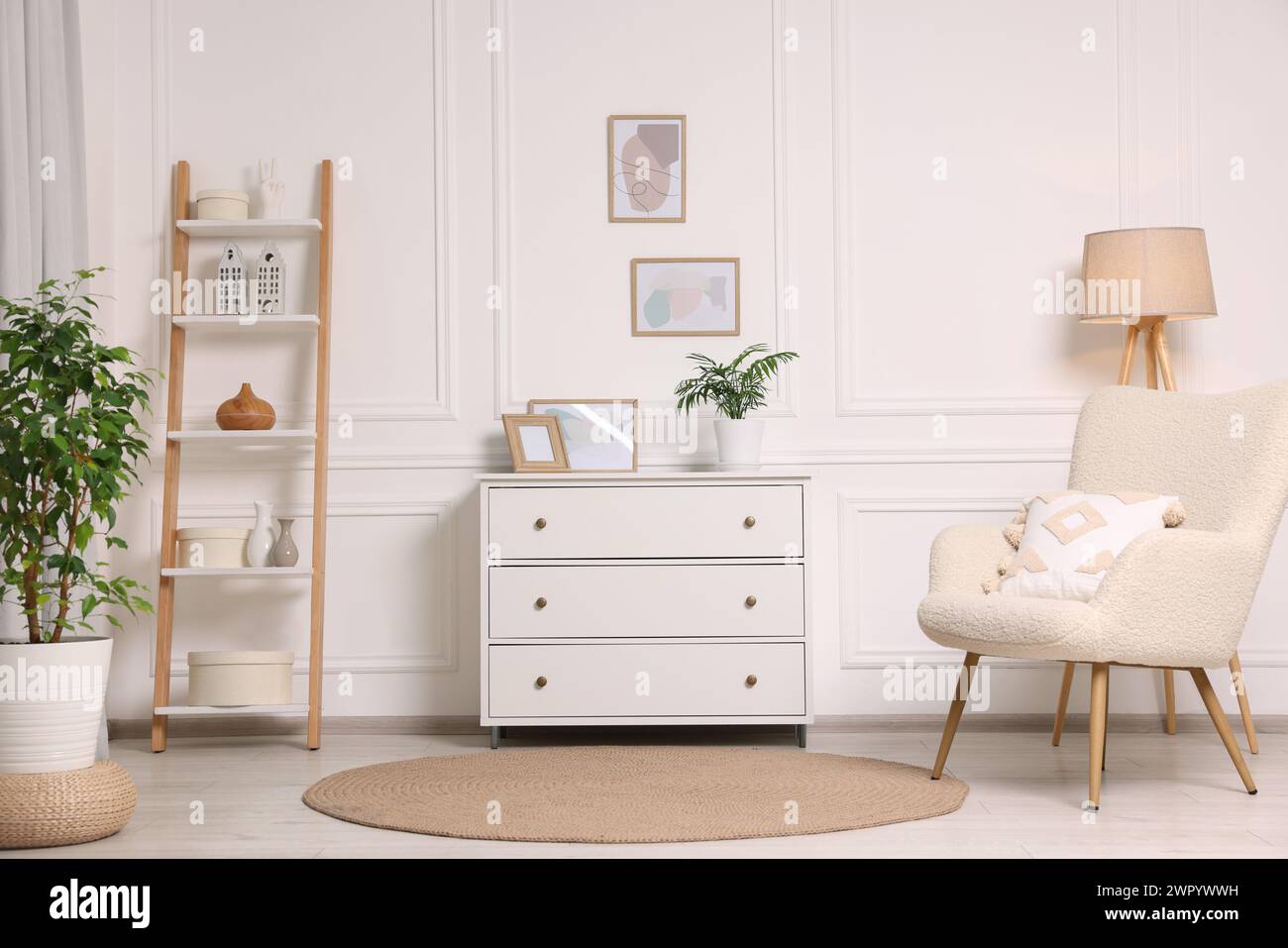 Picture frames hanging on white wall, chest of drawers and armchair in ...
