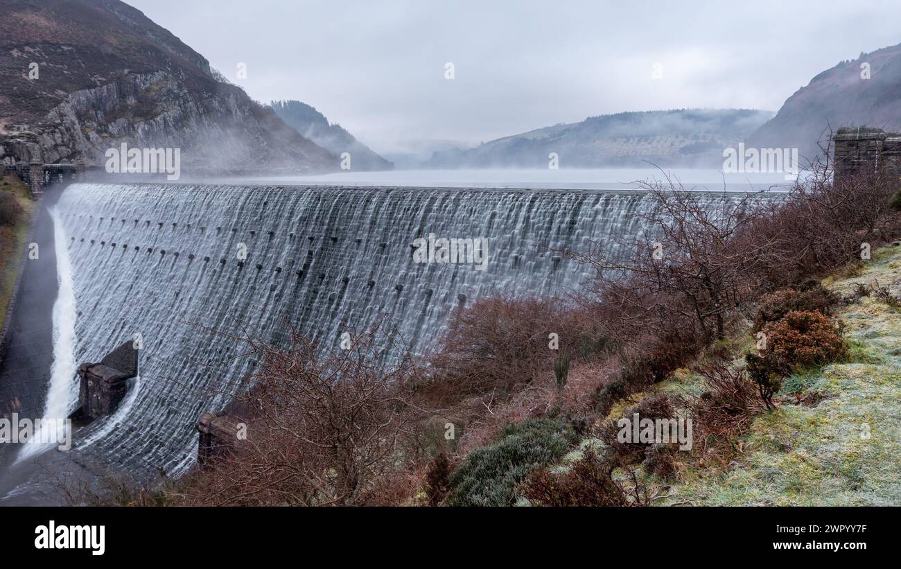 Water flowing over Caban Coch dam early morning with mist rising. One ...
