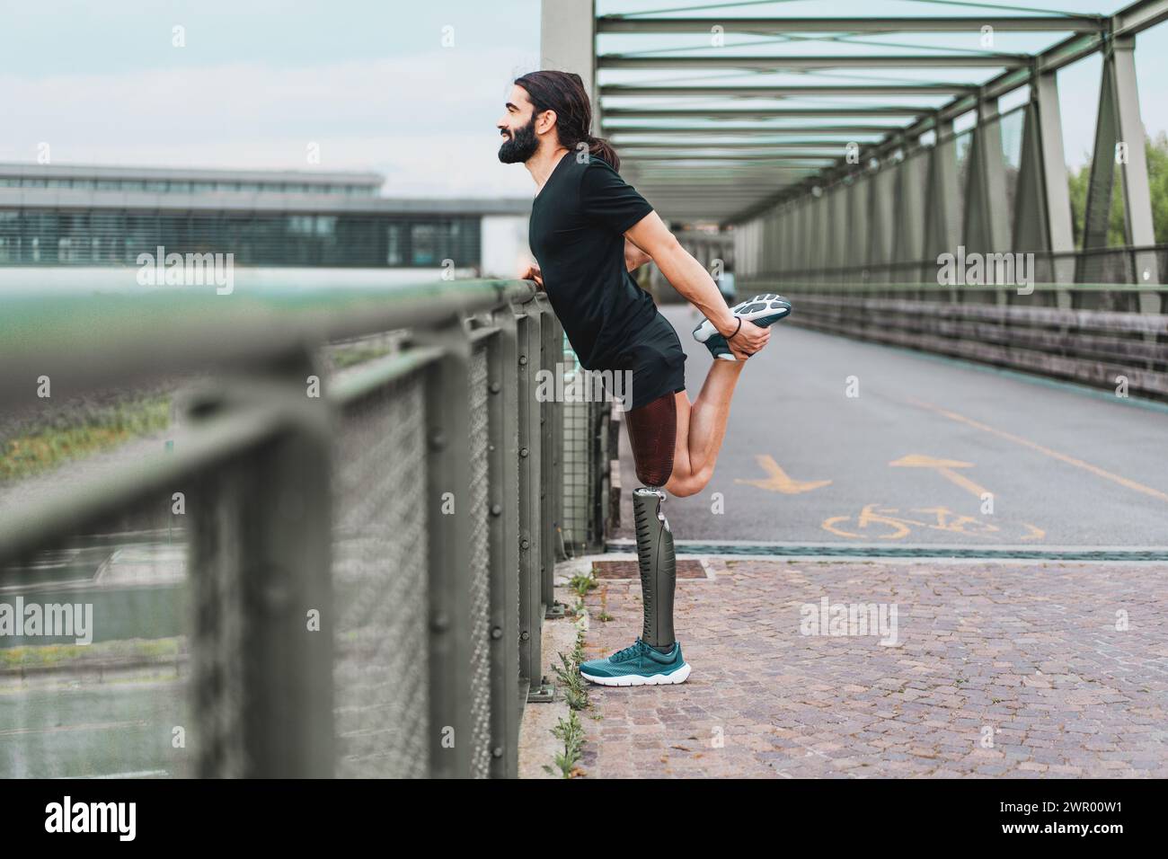 Adaptive athlete with leg prosthesis warming up on a bridge - Emphasis ... Adaptive athlete with leg prosthesis warming up on a bridge - Emphasis ...