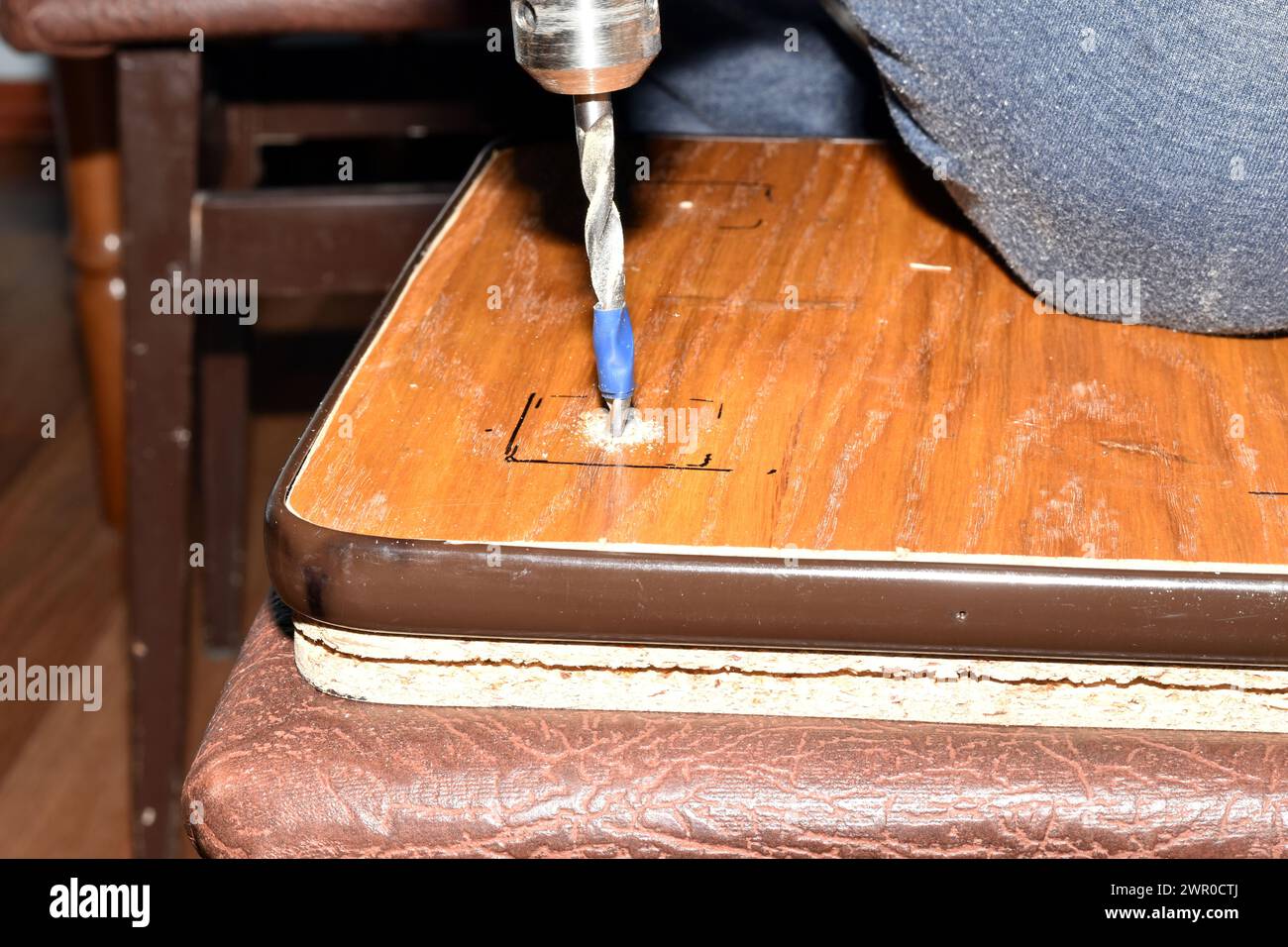 A carpenter uses a drill to drill a hole in a chair seat, holding the ...