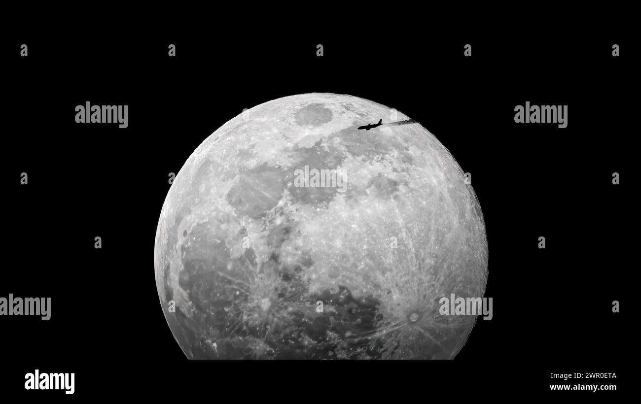 the moon rises against a deep black sky and an airplane flies by with a ...