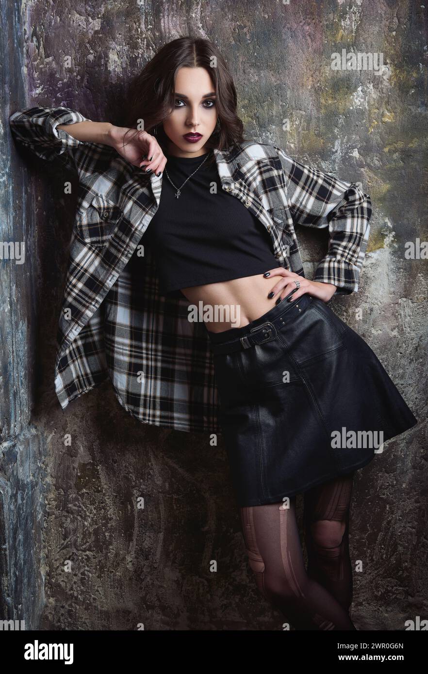 Indoor portrait of pretty grunge (rock) girl standing at the wall ...