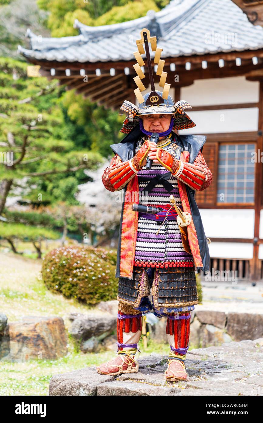 Japanese man standing in full samurai armour holding a microphone while ...