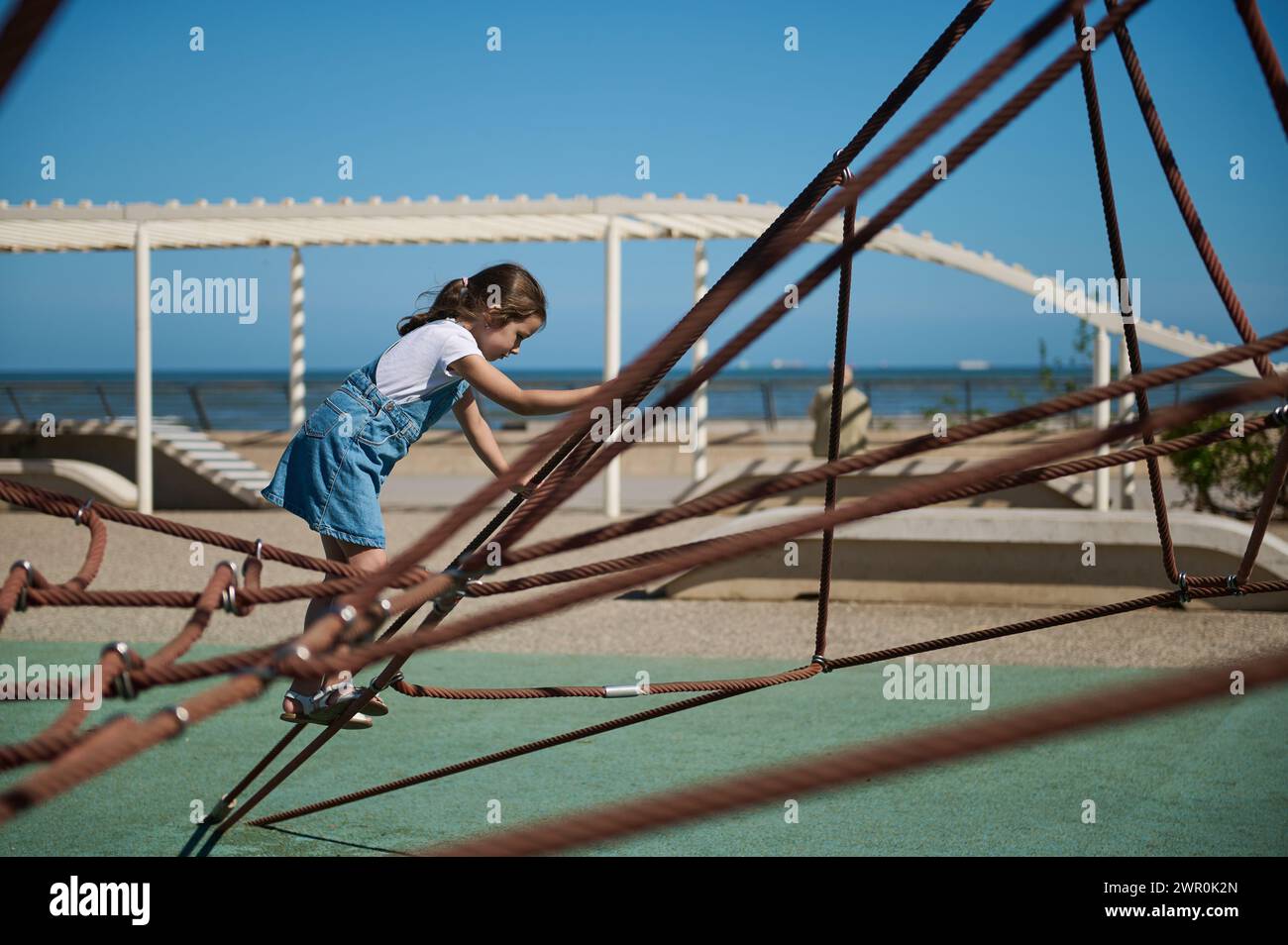 Adorable little girl climbing on a climbing net at the city playground ...