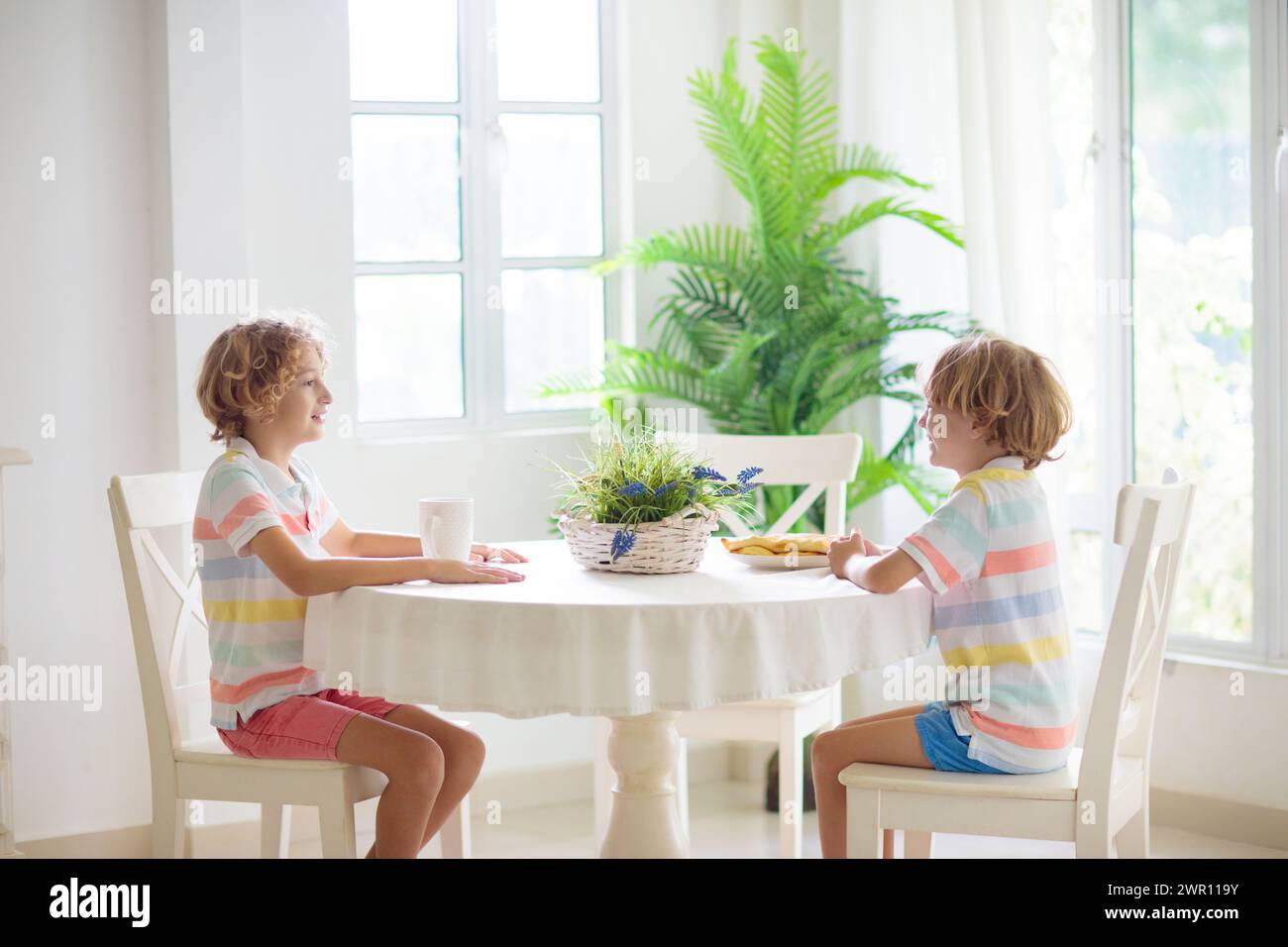 Kids eating breakfast in white kitchen. Children eat sandwich and drink ...