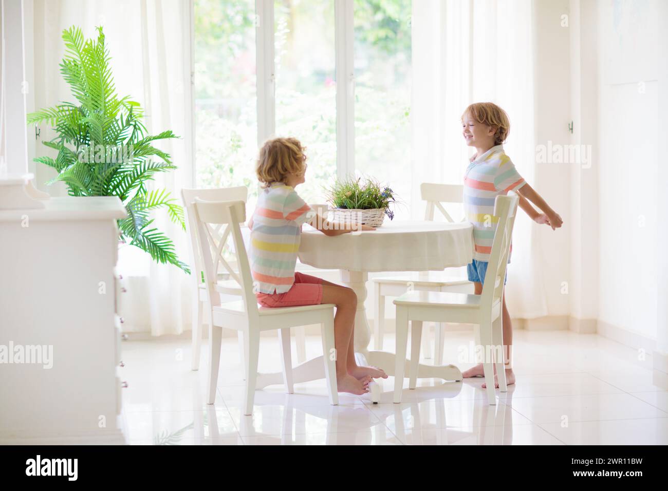 Kids eating breakfast in white kitchen. Children eat sandwich and drink ...