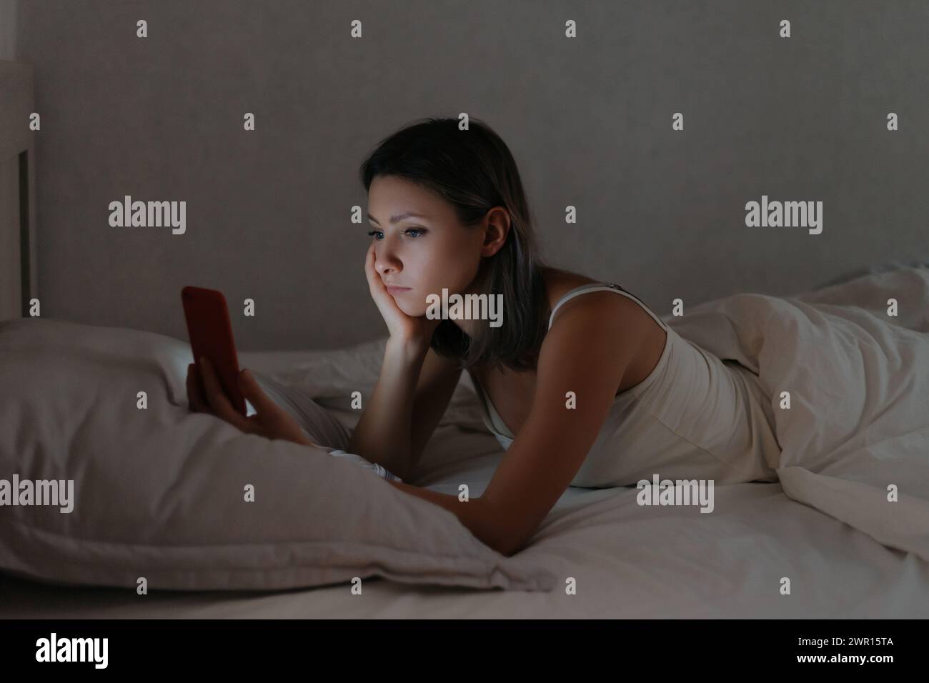 Female lying in bed and looking at her smartphone at night. Dependence ...
