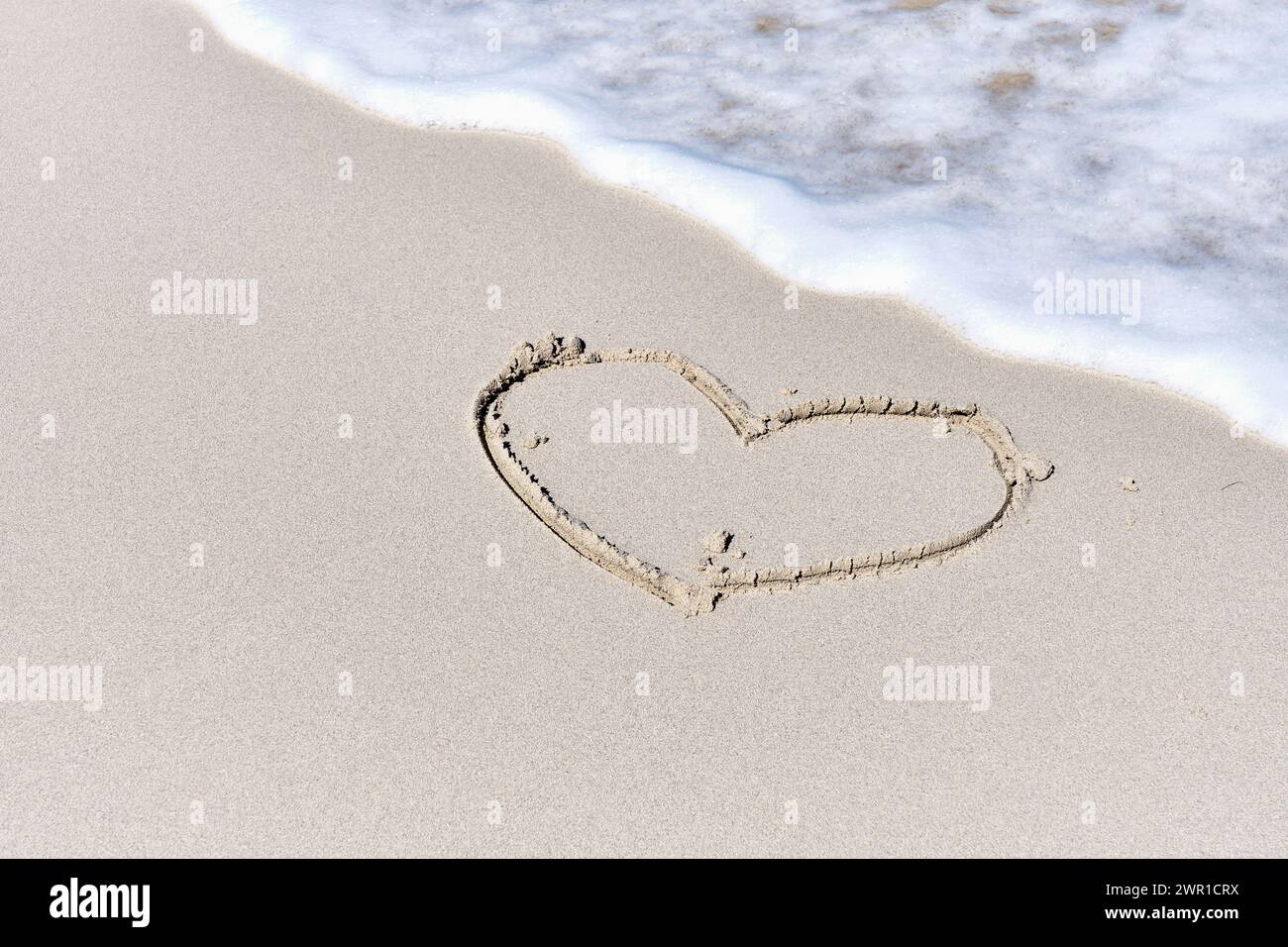 Foamy wave, washing over light sand with outline drawing of heart ...
