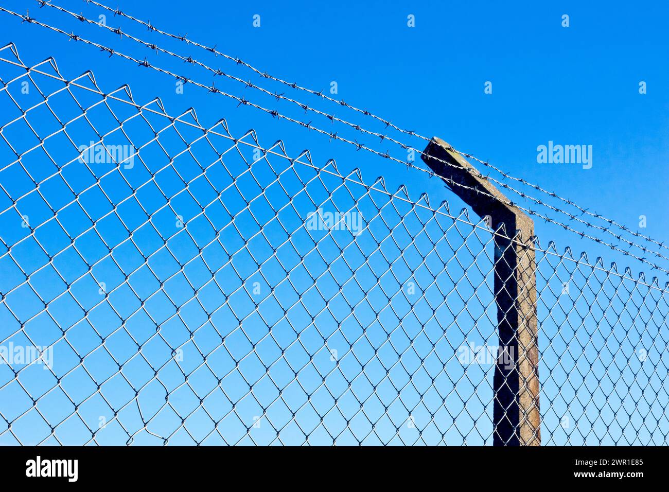 Close up of concrete fence post and chain link fence, topped with ...