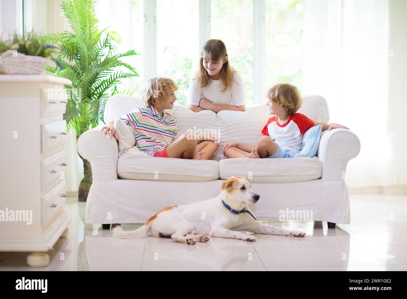 Kids play and watch tv on white couch. Children at home. Sunny family ...
