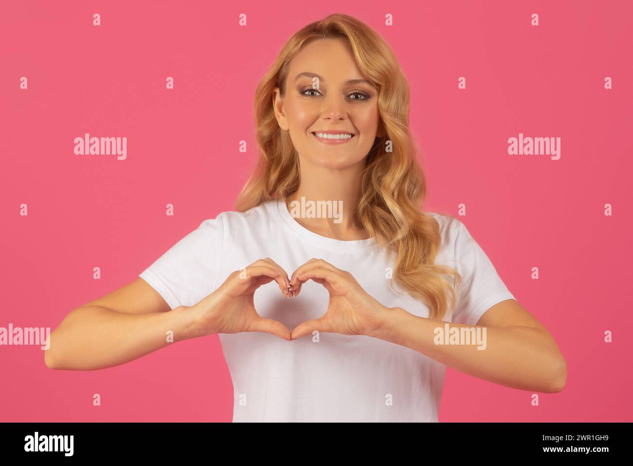 Pretty blonde lady forms a heart shape with fingers, studio Stock Photo ...