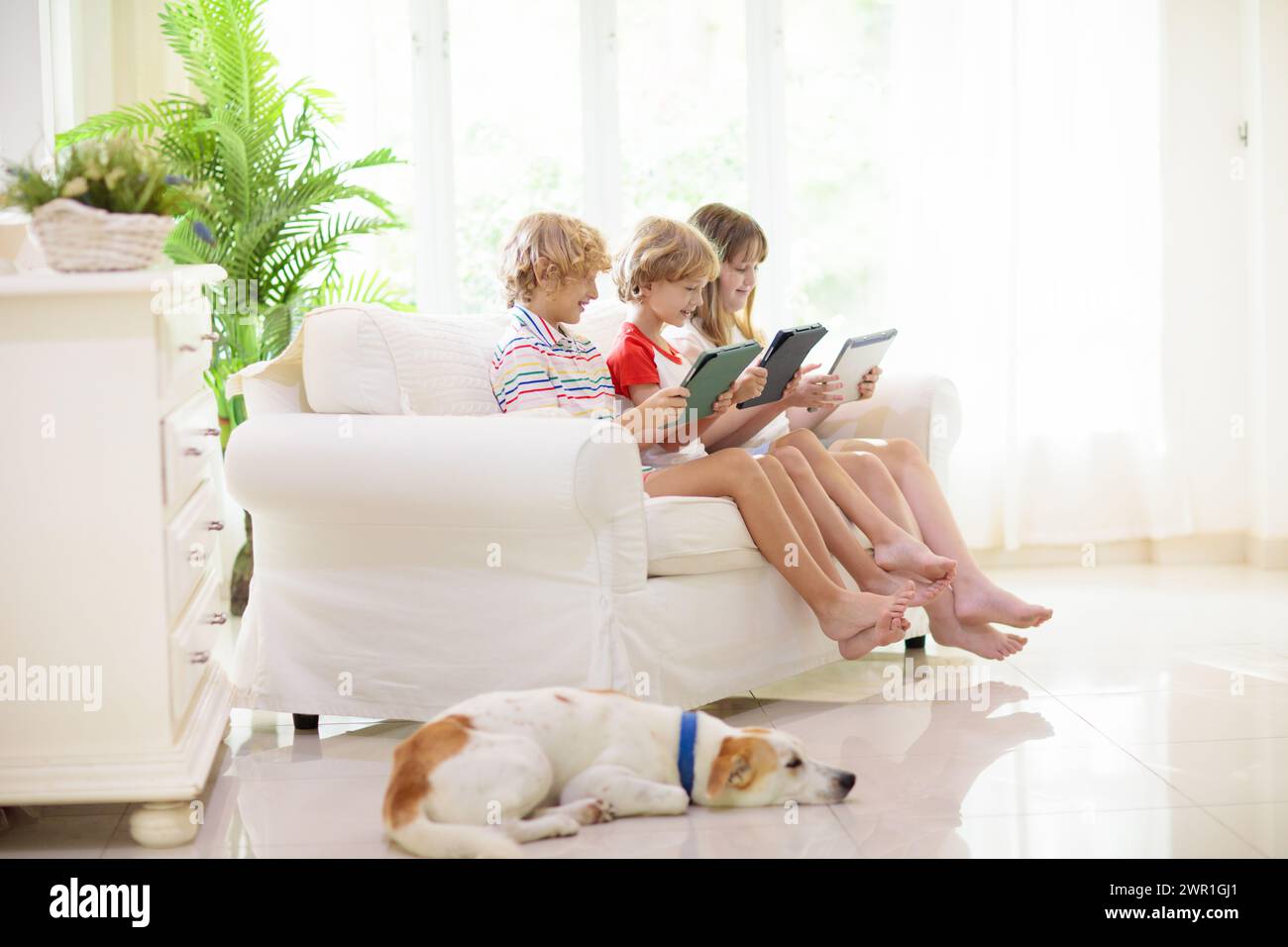 Kids play and watch tv on white couch. Children at home. Sunny family ...
