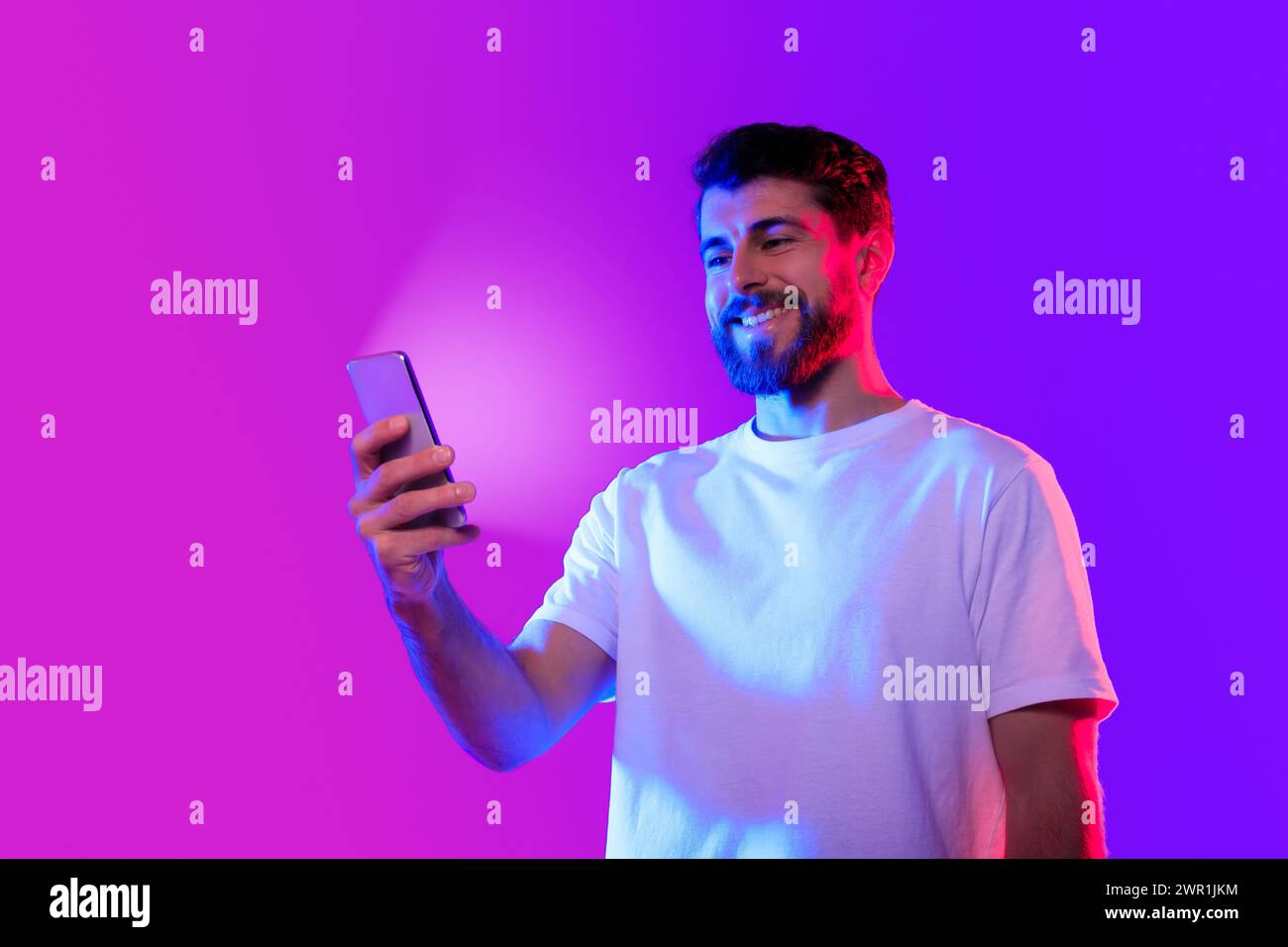 Cheerful caucasian man scrolling through a smartphone app, neon background Stock Photo - Alamy