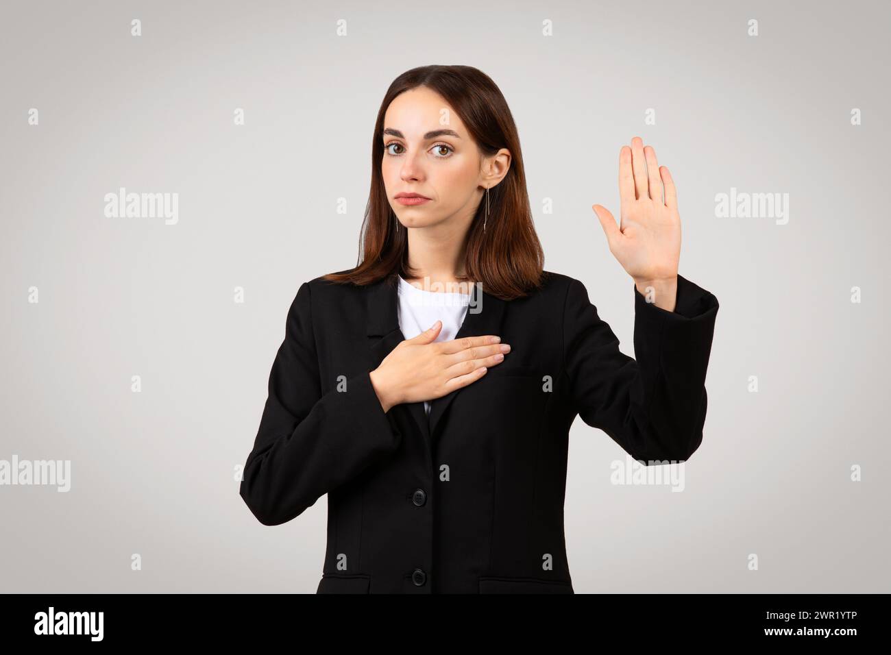 Solemn businesswoman in a black suit takes an oath with her right hand ...