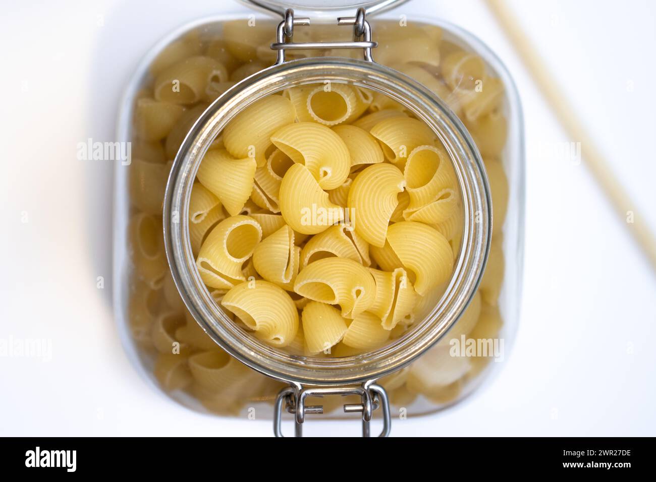Glass jar with dry pasta lumaconi on white background with blurry ...