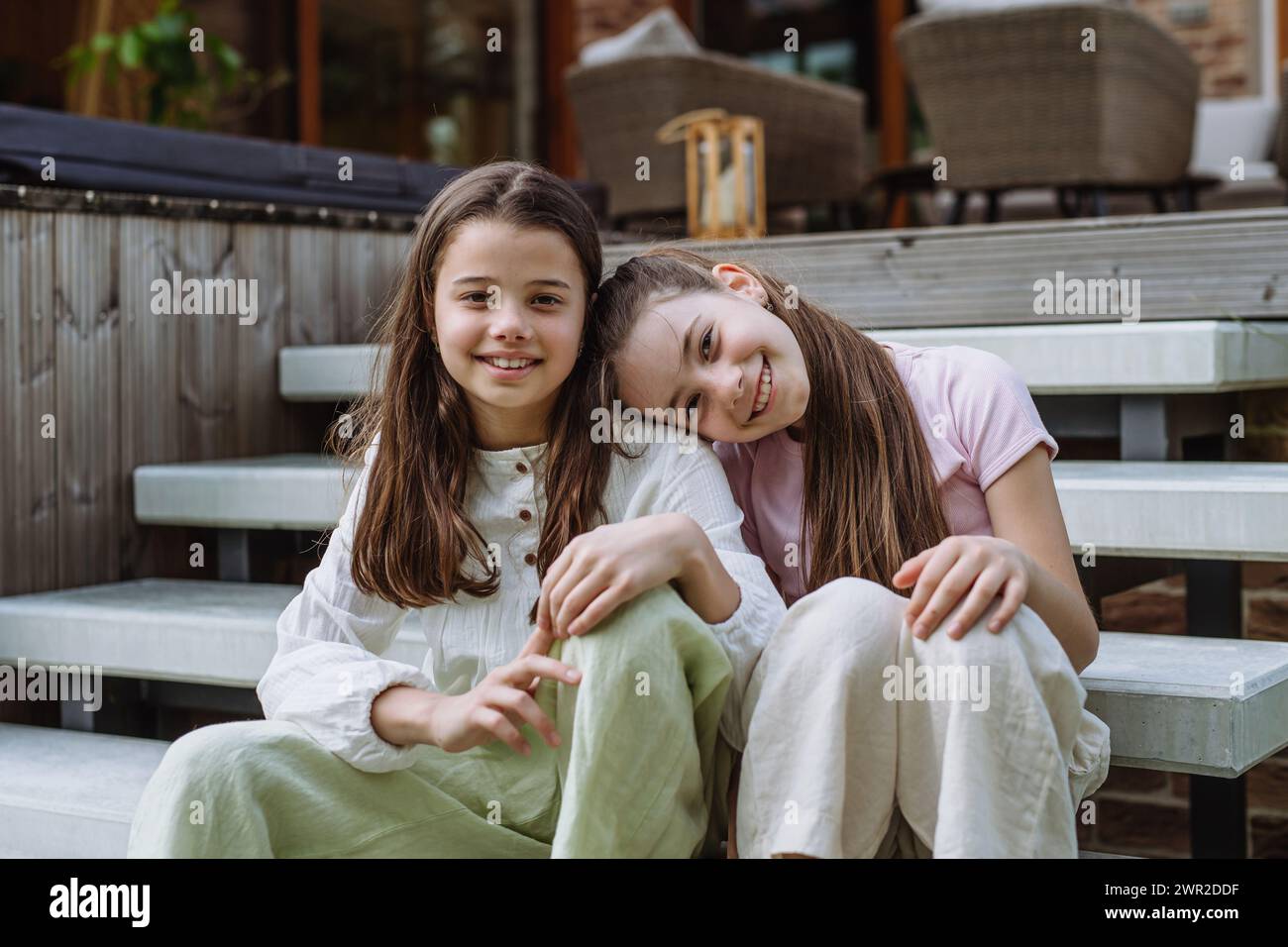 Two sisters sitting on stairs in front of house, embracing. Sisterly ...