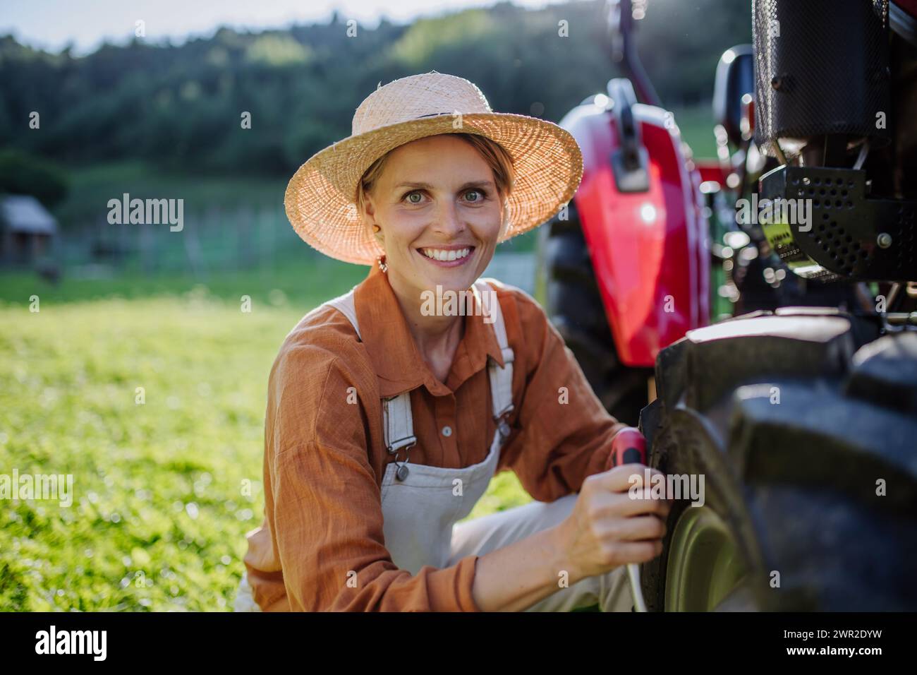 Female farmer fixing a wheel on a tractor. Progressive farmer working ...