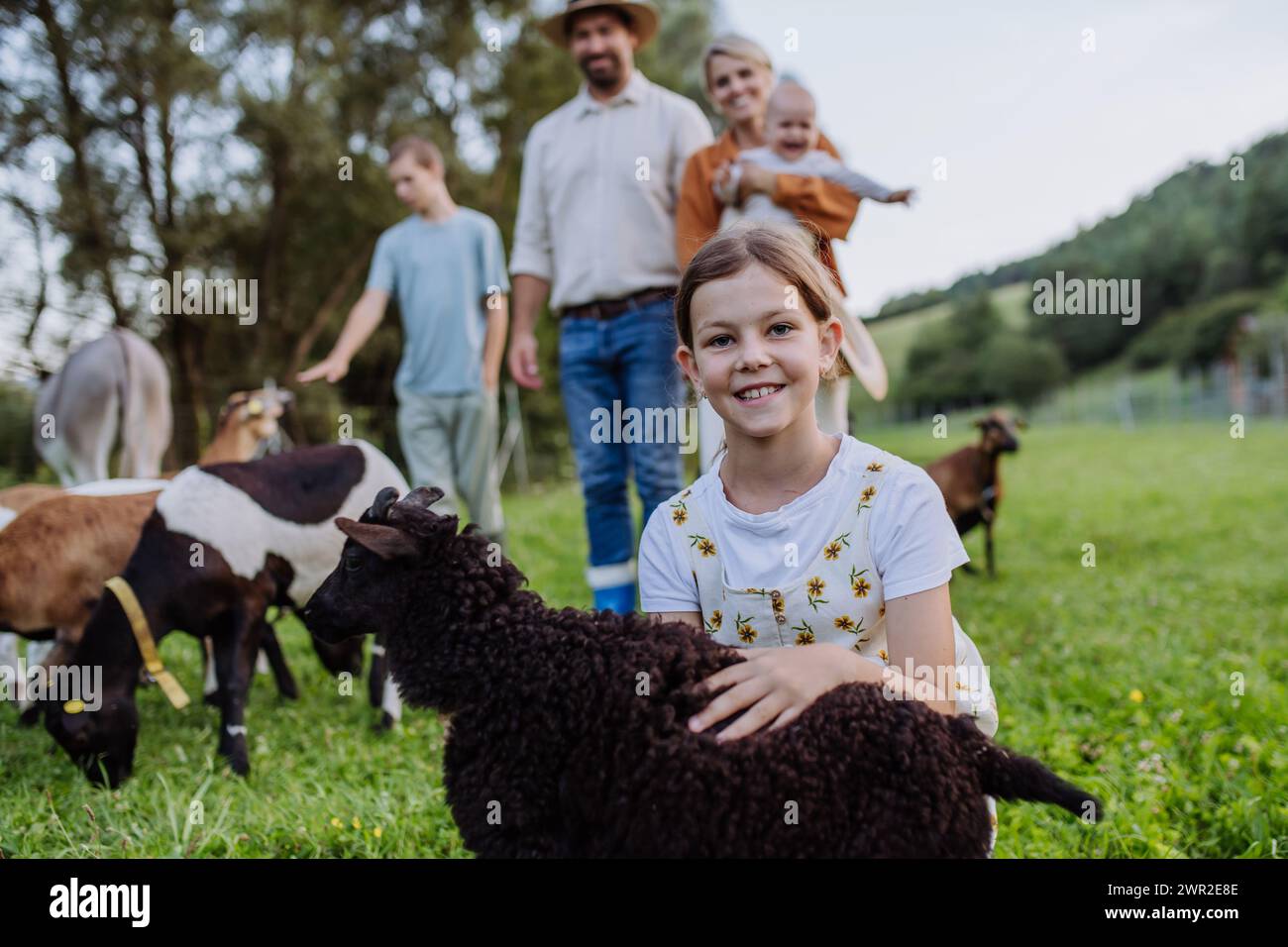 Portrait of farmer family petting donkey and goats on their farm. A ...