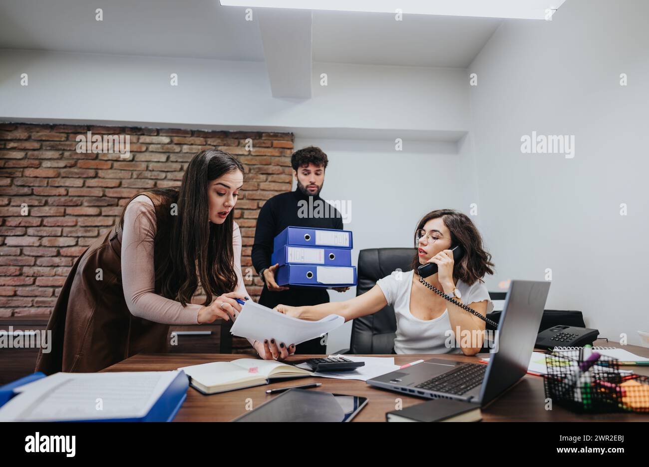 Busy office environment with focused team multitasking, woman on phone ...