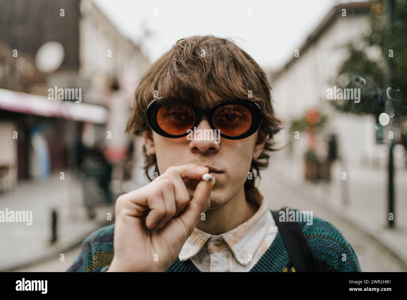 Fashionable young man in retro 90s style attire smokes cigarette on ...